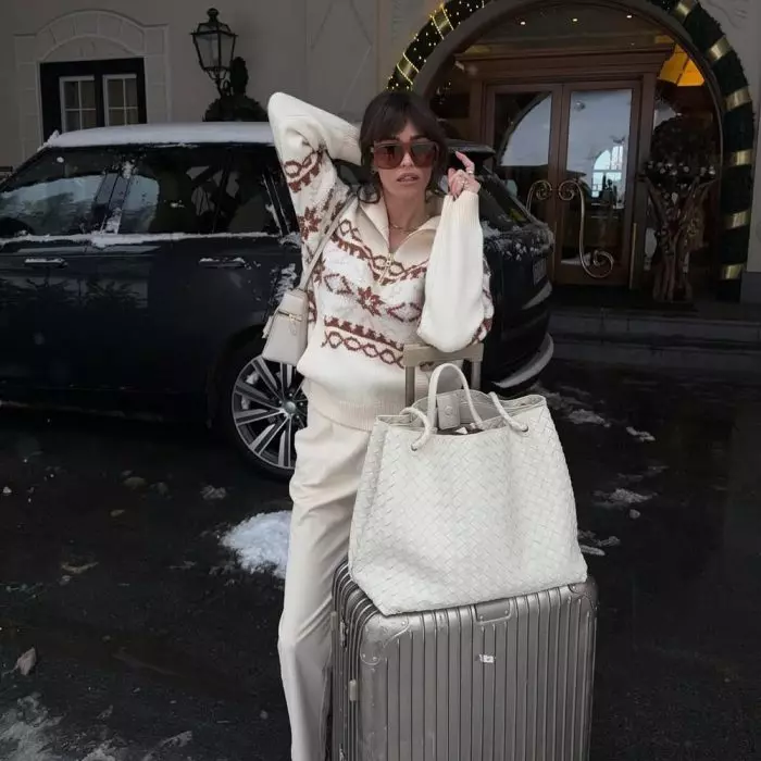 Chic winter travel outfit featuring a cream sweater with intricate brown patterns, beige wide-leg trousers, and a stylish Bottega Veneta woven tote.