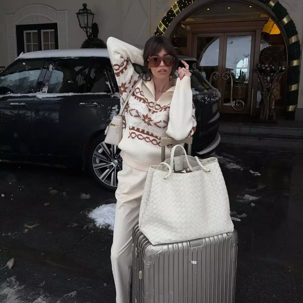Chic winter travel outfit featuring a cream sweater with intricate brown patterns, beige wide-leg trousers, and a stylish Bottega Veneta woven tote.
