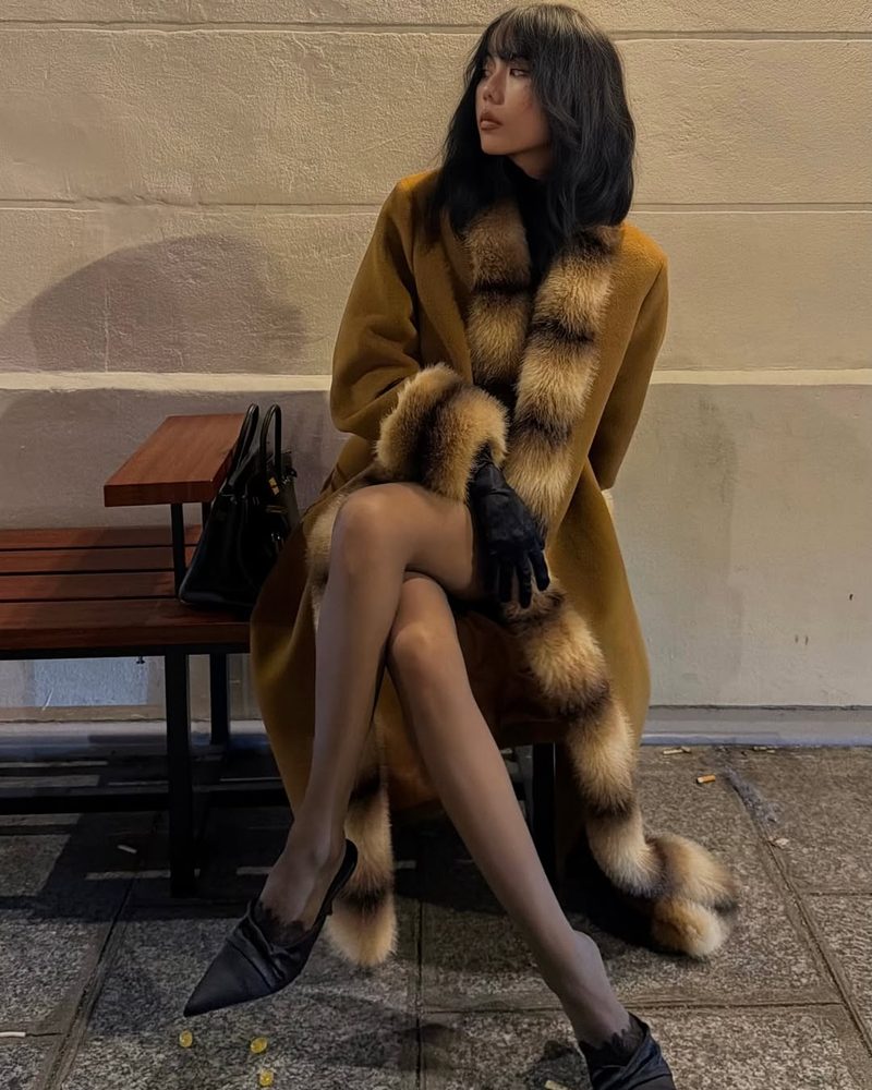 Street style look with caramel wool coat trimmed in plush fur%2C black gloves and pointed heels%2C styled on a city bench at night