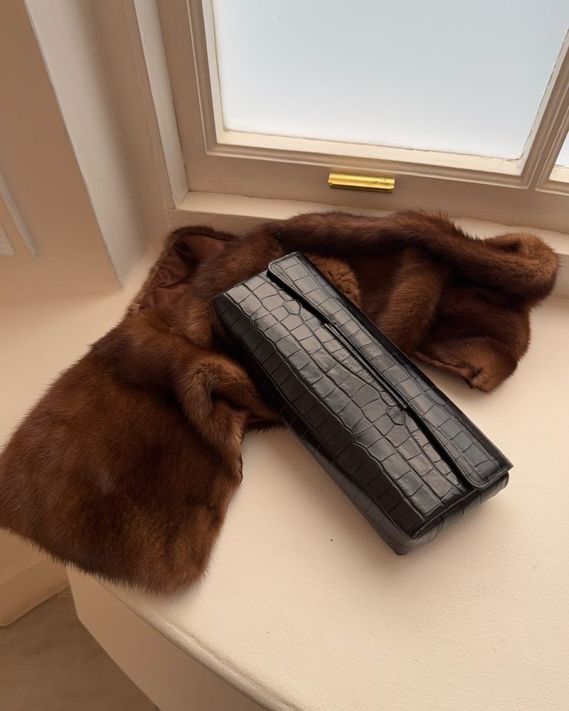 Sleek black crocodile print clutch bag styled atop a rich brown fur fabric%2C ideal for a chic evening outfit or stylish winter look
