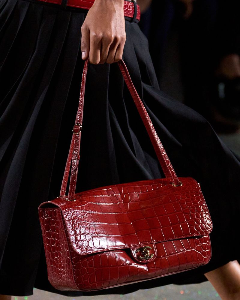 Chanel red crocodile leather shoulder bag with gold logo clasp paired with matching belt and black pleated skirt