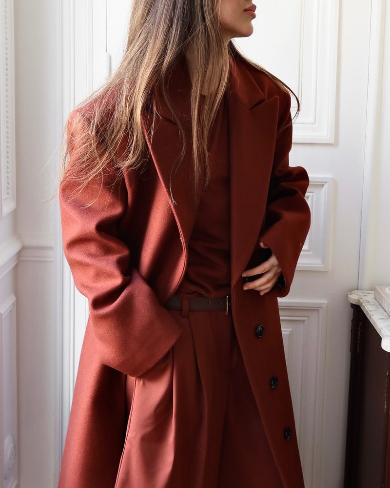 Chic autumn outfit featuring a tailored rust wool coat layered over a matching turtleneck and trousers%2C accented by a brown belt