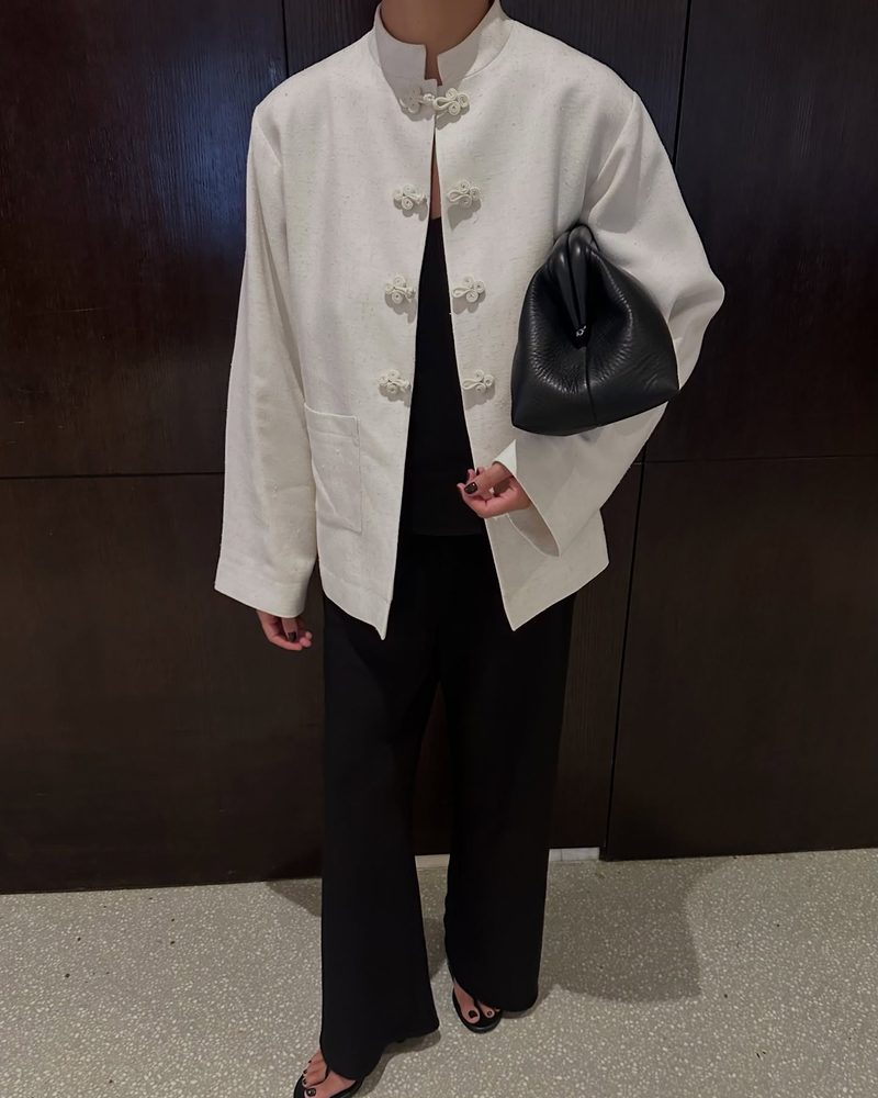 Mandarin collar jacket in cream fabric with decorative buttons%2C paired with a black top and wide-leg trousers%2C accessorized with a black bag