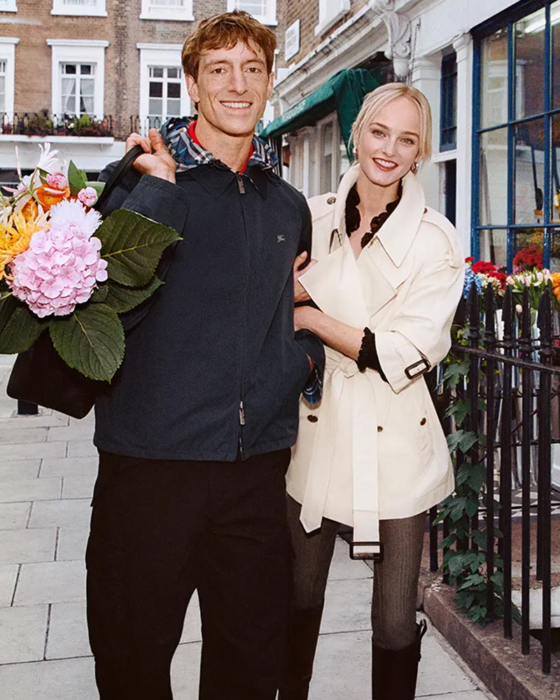 Couple styled in fall outerwear%2C featuring a cream trench coat and black jacket with bouquet%2C walking on a charming city street