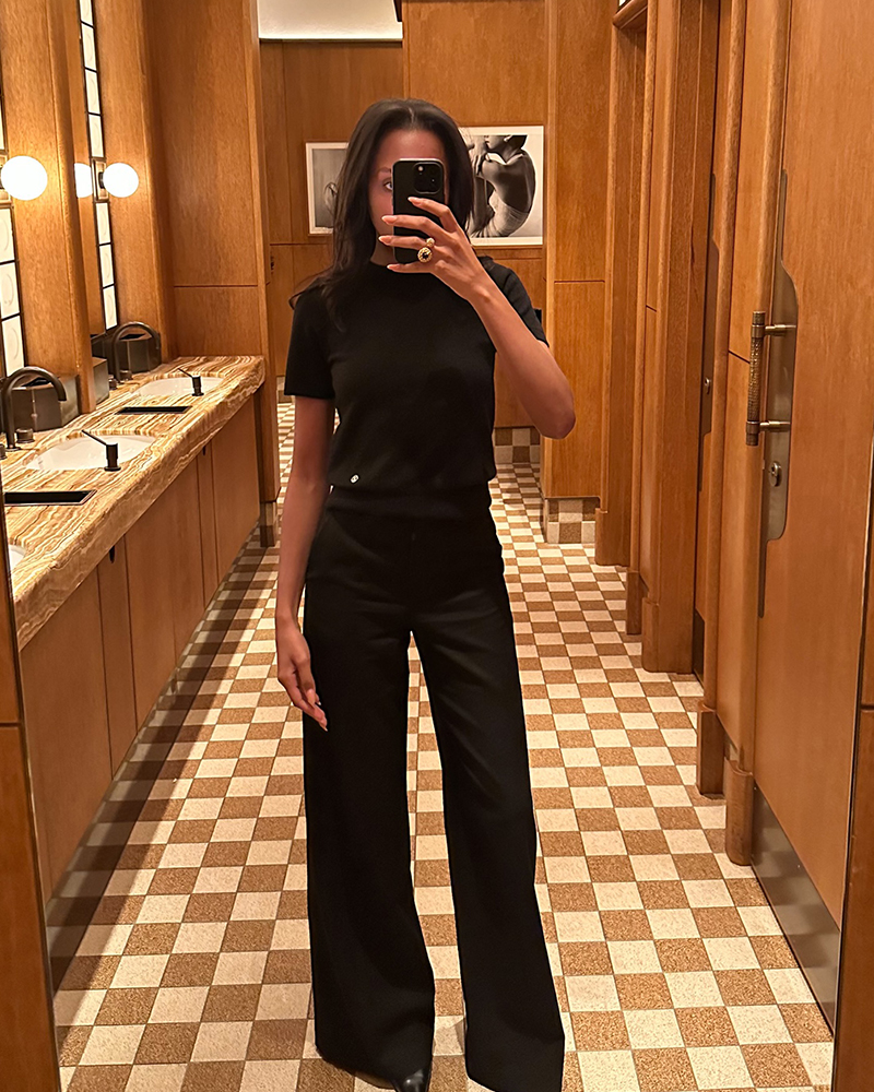 Minimalist black outfit featuring a fitted short-sleeve T-shirt and wide-leg trousers%2C styled in a warm wood-paneled restroom