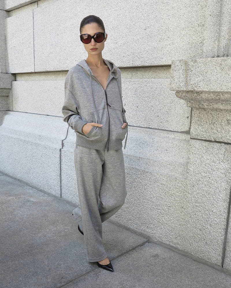 Street-style look featuring a gray zip-up hoodie and wide-leg sweatpants with oversized sunglasses%2C styled against a stone wall