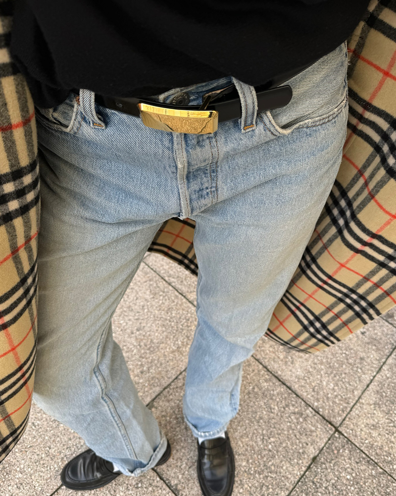 Close-up of light wash straight-leg jeans with black leather belt and loafers%2C styled with plaid coat on city sidewalk