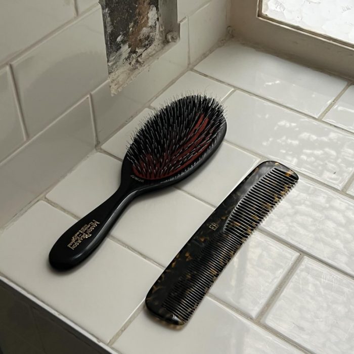Mason Pearson hairbrush and tortoiseshell comb grooming tools styled on a white tiled bathroom windowsill in soft natural light