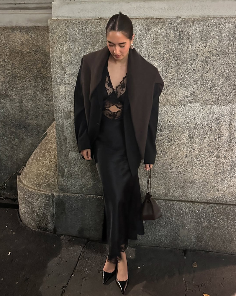Street style look with black lace slip dress and oversized blazer%2C styled with pointed heels and mini bag against stone walls