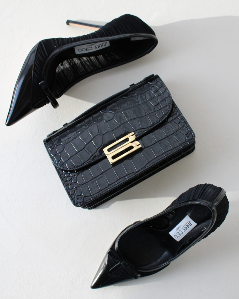 Jimmy Choo black croc-embossed clutch styled with pleated leather pumps%2C arranged flat on a clean white surface