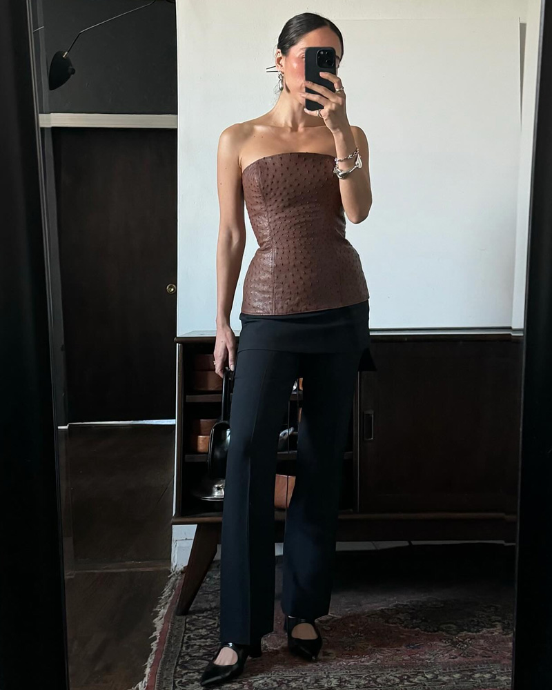 Mirror selfie outfit featuring a brown ostrich leather strapless top%2C black tailored trousers%2C and flats in a minimalist interior