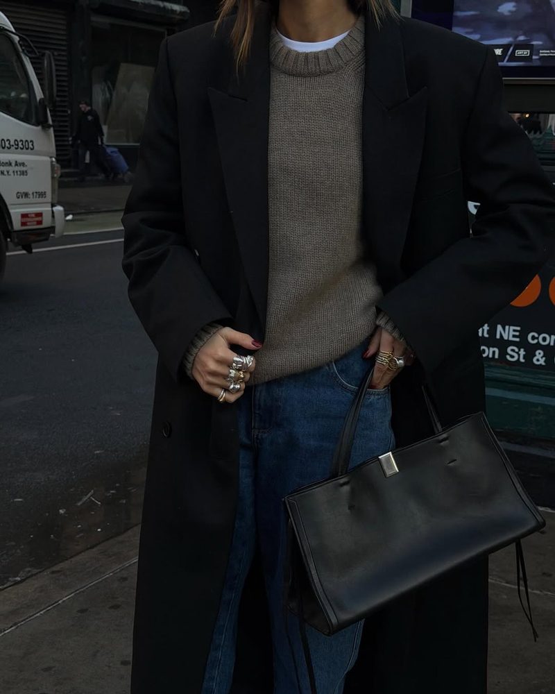 Crewneck sweater outfit with a taupe knit%2C oversized black coat%2C straight-leg jeans%2C and a sleek black leather shoulder bag
