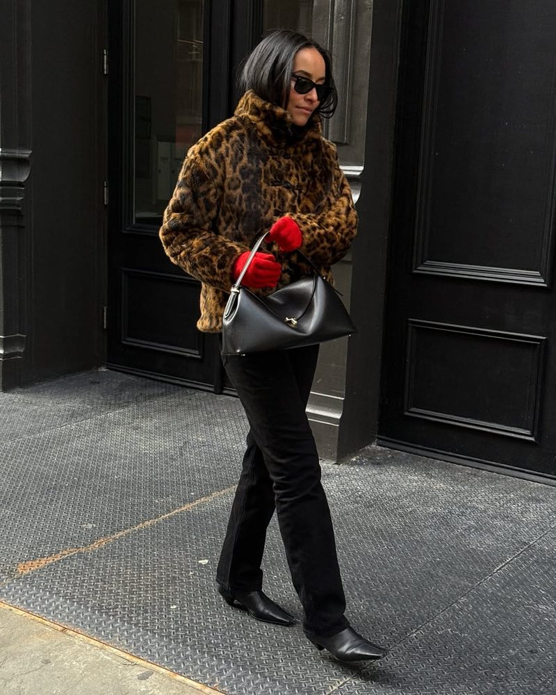 Chic leopard print faux fur jacket paired with sleek black jeans and stylish black ankle boots%2C accented by vibrant red gloves and a designer handbag.