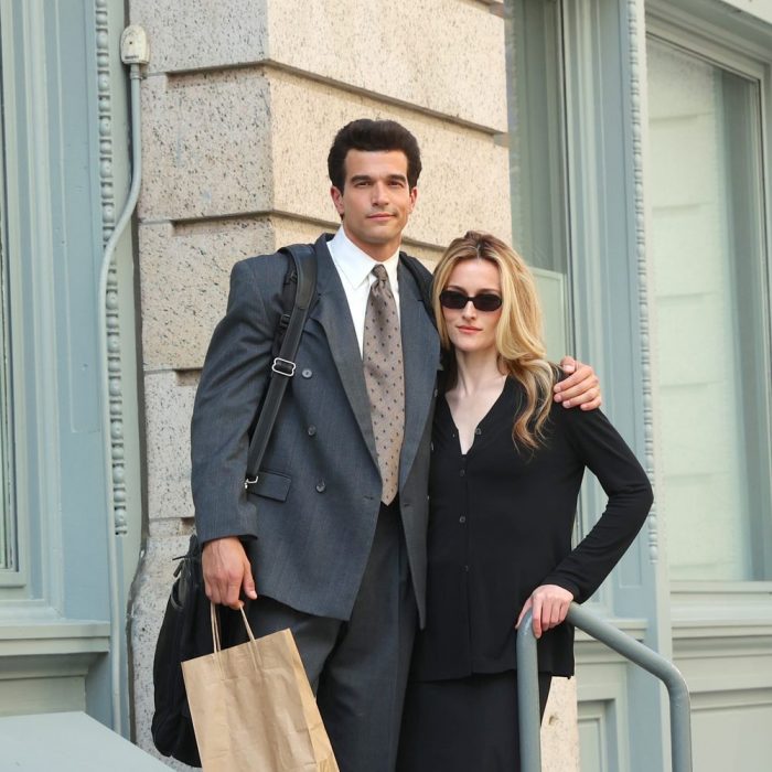 Sophisticated couple showcasing office-ready looks: the man in a gray pinstripe suit with a patterned tie, the woman in a chic black blouse and skirt with stylish sunglasses.