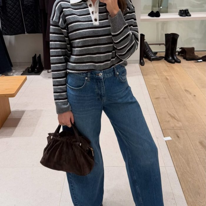 Striped gray and white polo sweater paired with high-waisted barrel leg jeans, complemented by a stylish brown suede bag and black loafers.