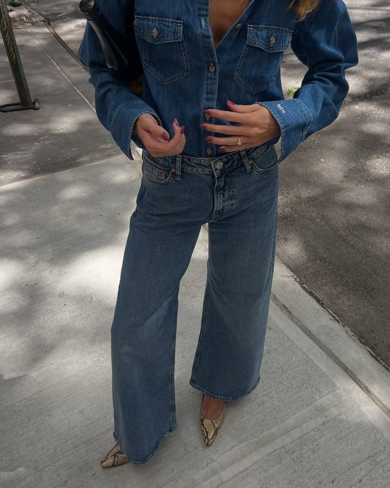 Chic Canadian tuxedo featuring a fitted denim shirt paired with wide-leg blue jeans and stylish snake-print heels.