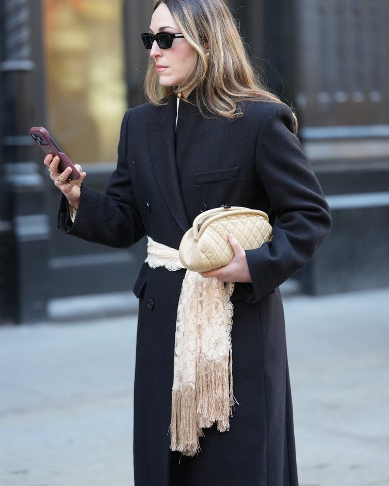 Chic ensemble featuring a black double-breasted coat%2C a beige quilted clutch%2C and a delicate lace scarf%2C perfect for NYFW elegance.