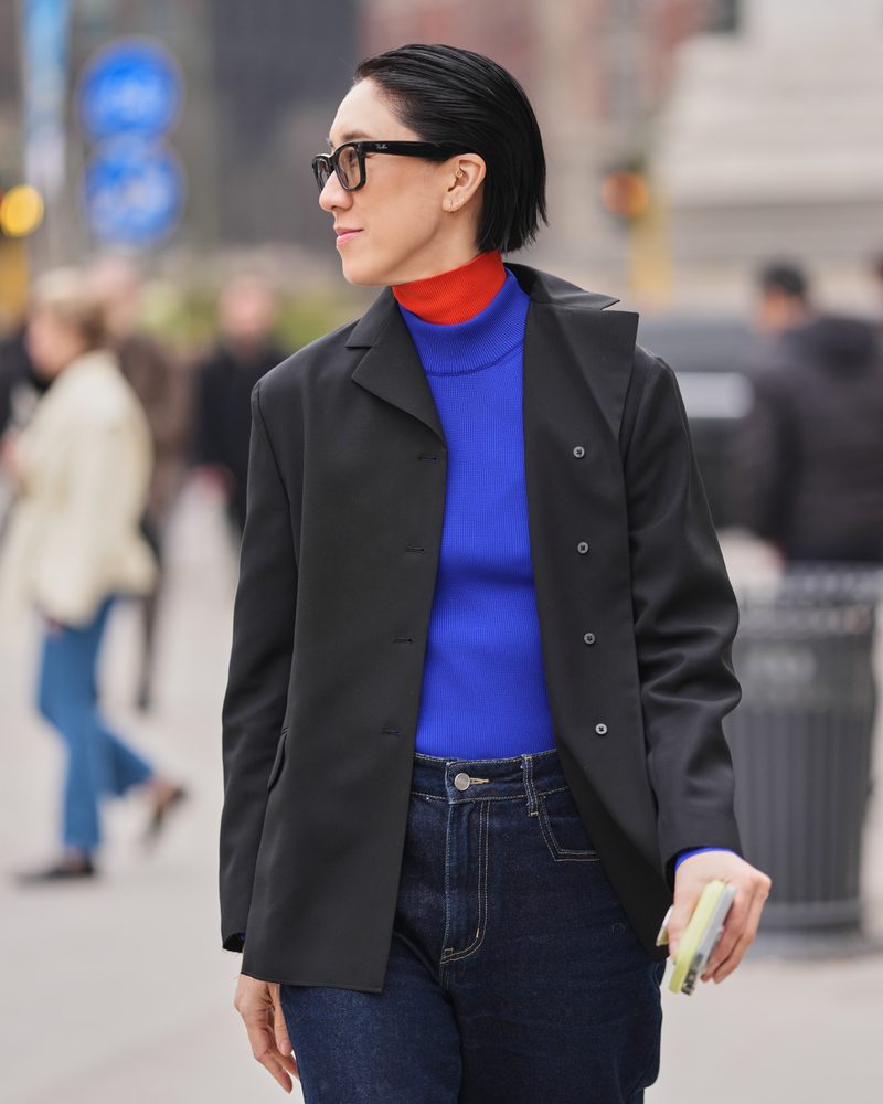 Chic street style featuring a woman in a black oversized blazer layered over a vibrant blue sweater%2C paired with high-waisted denim and statement glasses.