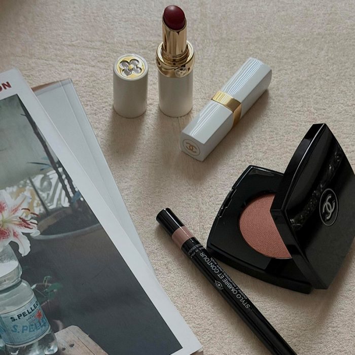 Chanel makeup flat lay featuring lipstick, blush compact, and lip liner, styled beside art books on linen