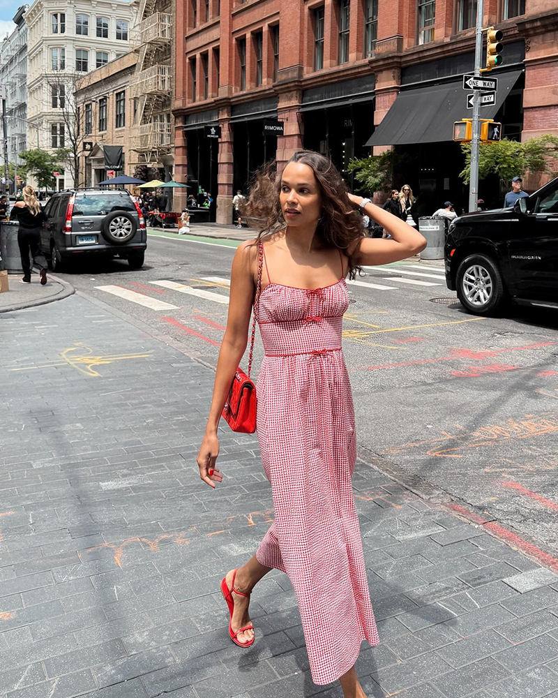 Street style look in a red gingham sundress with red mini bag and strappy sandals on a city crosswalk