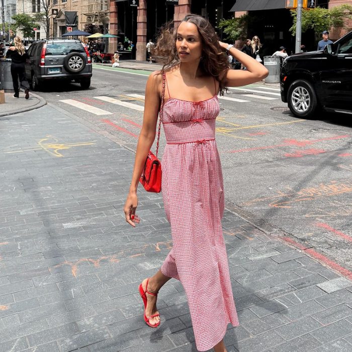 Street style look in a red gingham sundress with red mini bag and strappy sandals on a city crosswalk