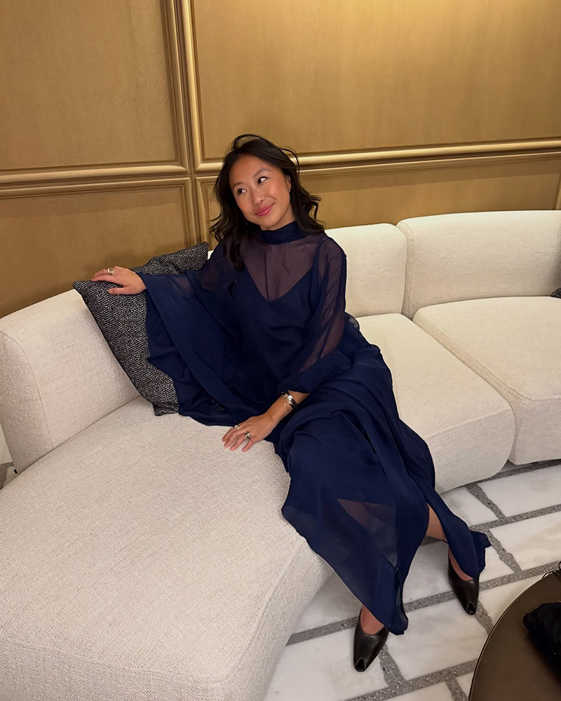 Model lounging on cream sofa in navy sheer chiffon maxi dress and black pumps%2C styled in an elegant hotel lounge