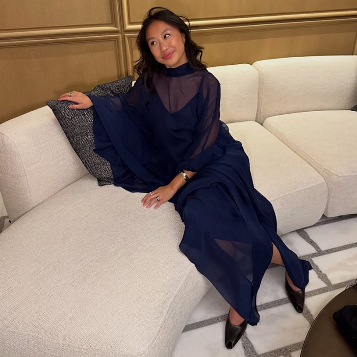Model lounging on cream sofa in navy sheer chiffon maxi dress and black pumps, styled in an elegant hotel lounge