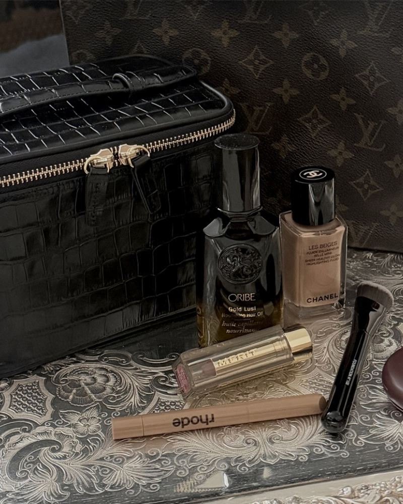 Chanel Les Beiges foundation and Oribe Gold Lust hair oil beside black croc travel makeup bag on embossed tray