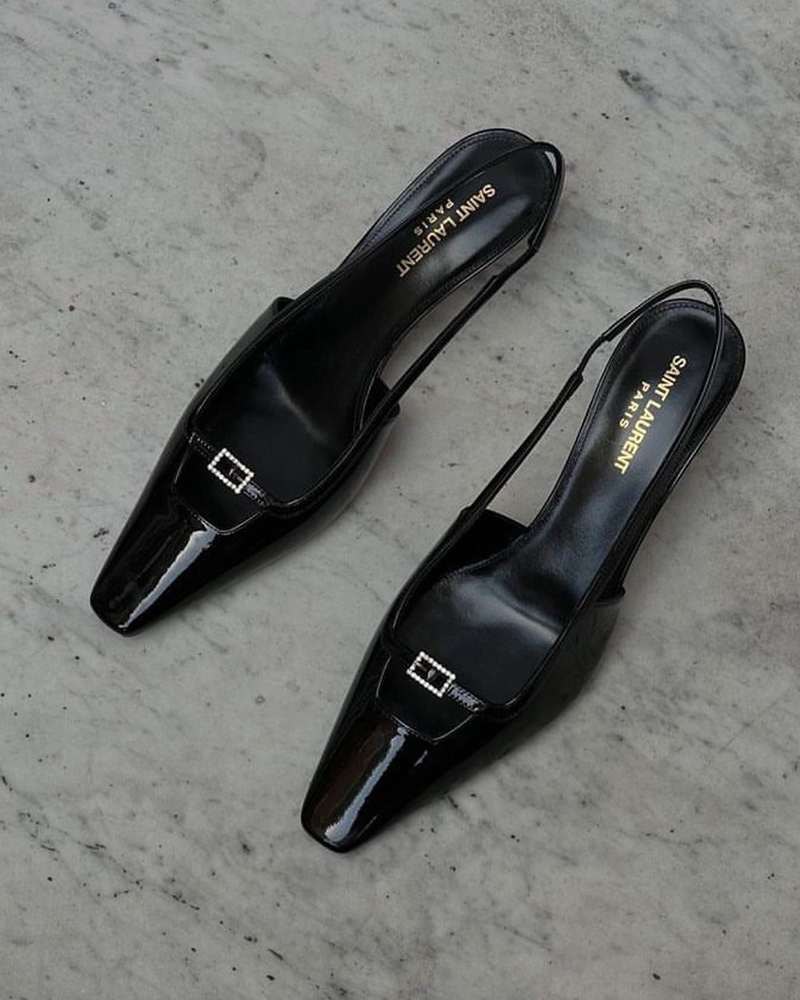 Saint Laurent patent leather slingback pumps with pointed toe and silver buckle%2C styled on a minimalist stone surface