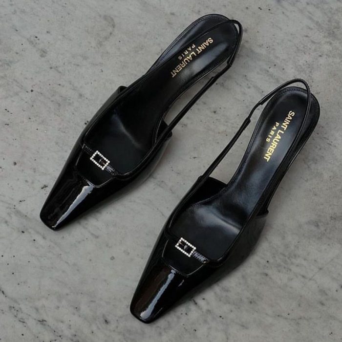 Saint Laurent patent leather slingback pumps with pointed toe and silver buckle, styled on a minimalist stone surface