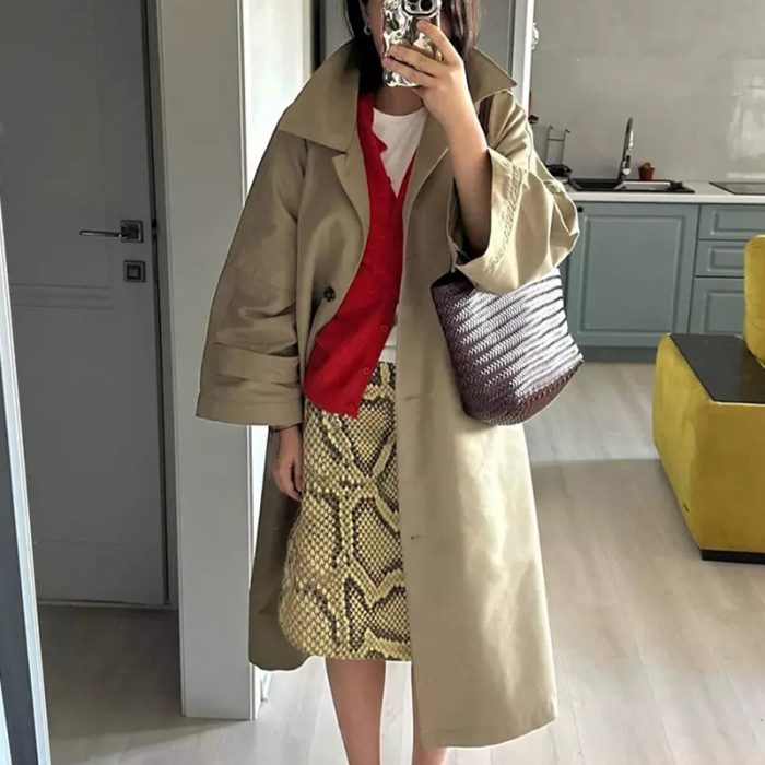 Chic spring outfit showcases a khaki trench coat over a vibrant red cardigan, patterned yellow snakeskin skirt, and pointed nude heels.