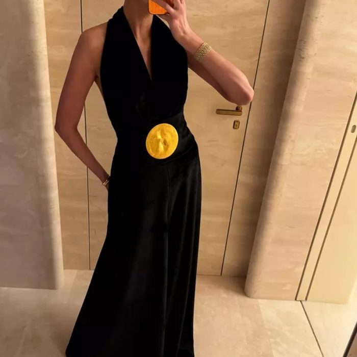 Elegant black halter gown featuring a dramatic plunging neckline and a bold gold circular belt, styled with statement earrings.