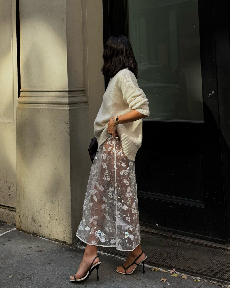 Street style look with cream sweater and sheer floral midi skirt paired with black heeled sandals on city sidewalk