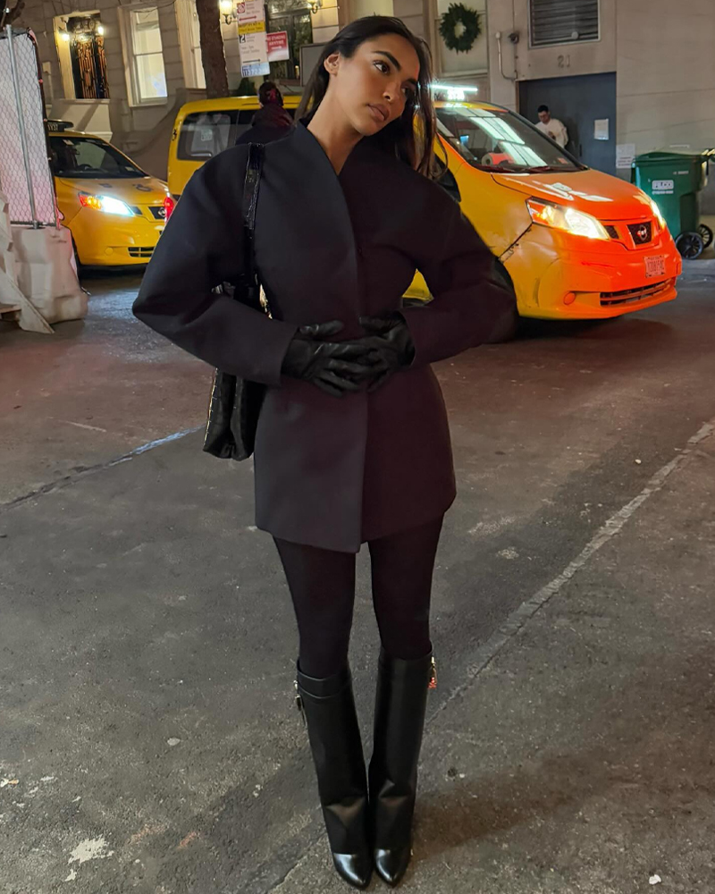 Model wearing structured black blazer%2C gloves%2C and knee-high boots on a city street with yellow taxis at night