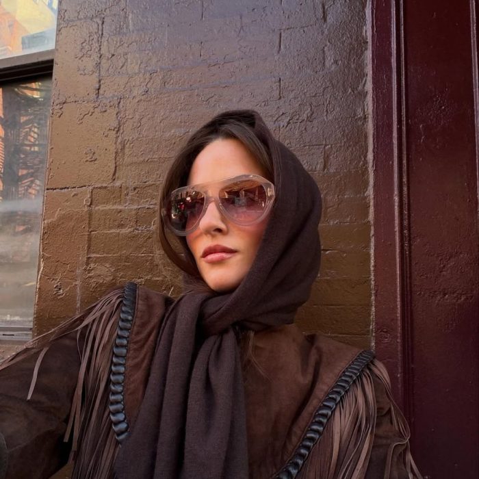 Chic bohemian look featuring a fringed brown suede top, oversized sunglasses, and a matching brown scarf against a rustic backdrop.
