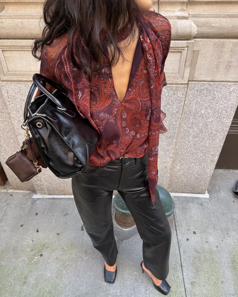 Burgundy paisley print blouse layered over sleek black leather pants%2C accessorized with a mini black handbag%2C perfect for fall styling