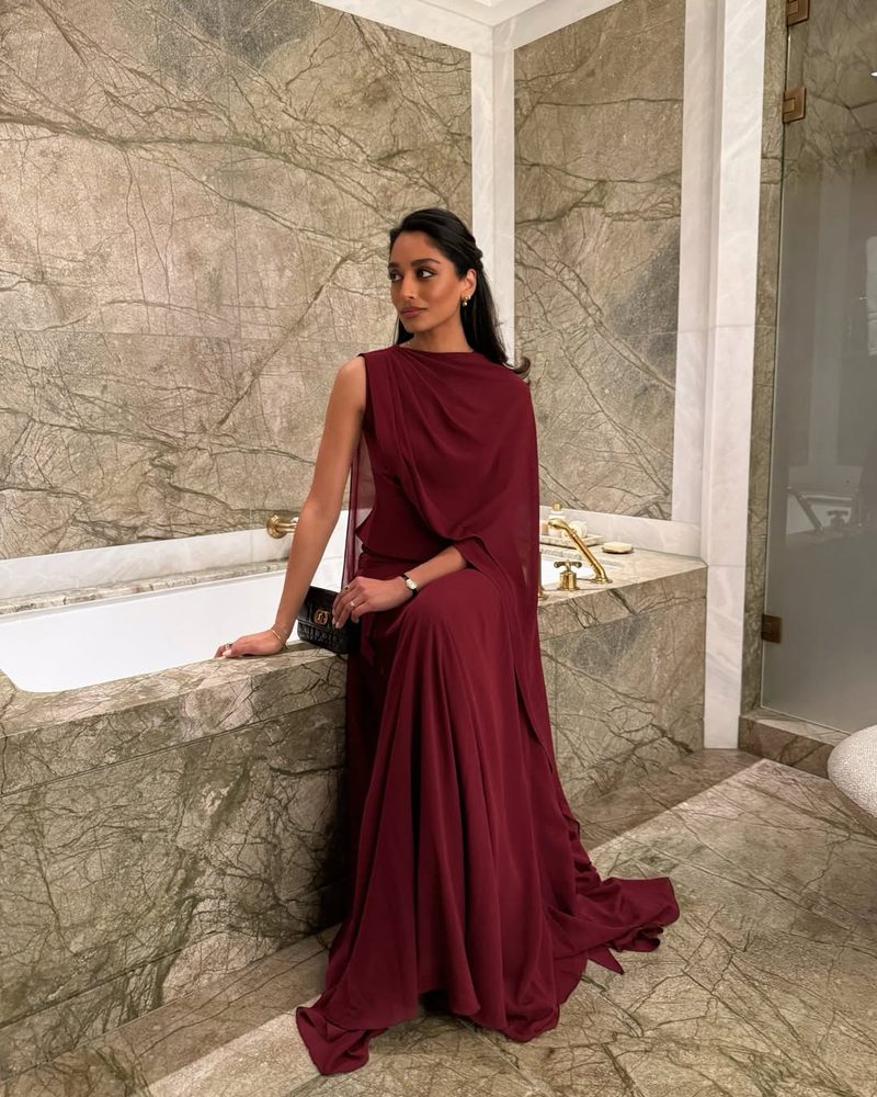 Elegant burgundy evening gown drapes gracefully on a model%2C complemented by a chic black handbag against a luxurious marble backdrop