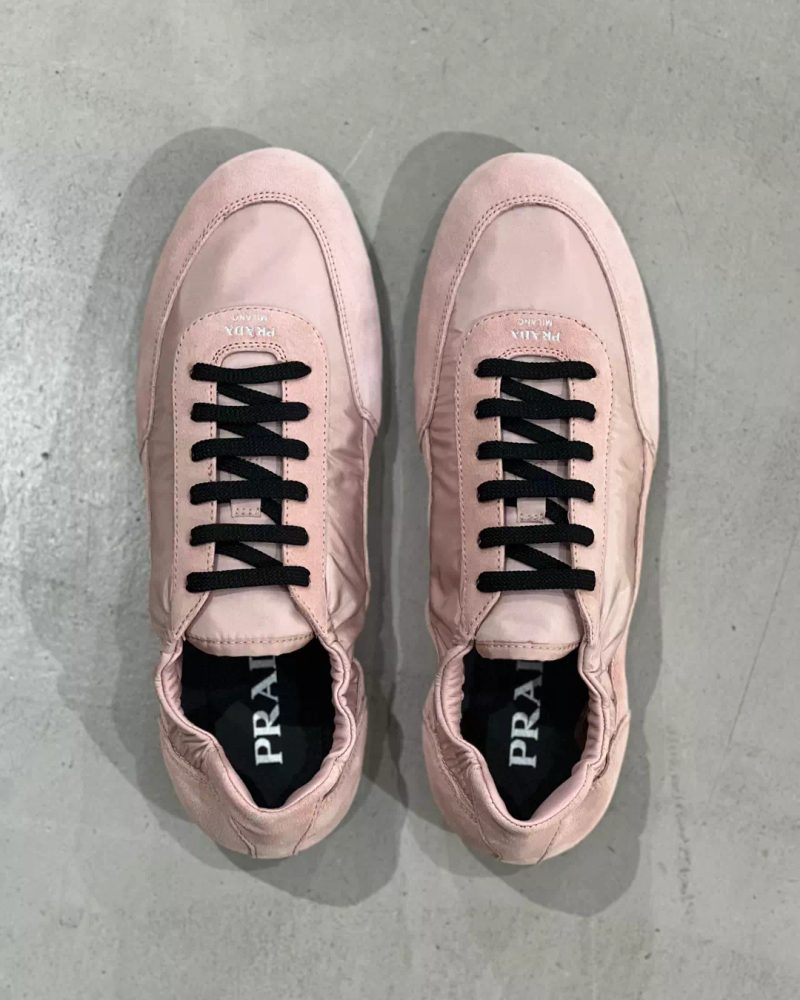 Prada pale pink leather sneakers with black laces%2C minimalist low-top trainers in soft pastel tone on neutral background