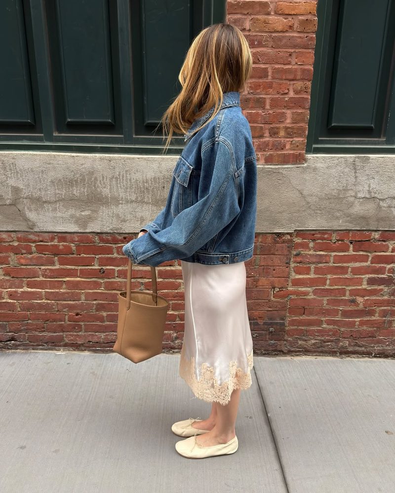 Denim jacket layered over silk lace trim slip skirt with ballet flats and tan tote bag for effortless spring street style
