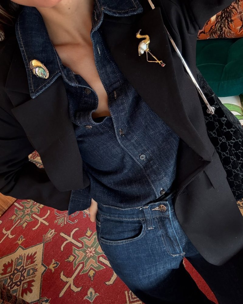 Chic Canadian tuxedo look featuring a denim button-up shirt layered under a tailored black blazer%2C accessorized with unique brooches