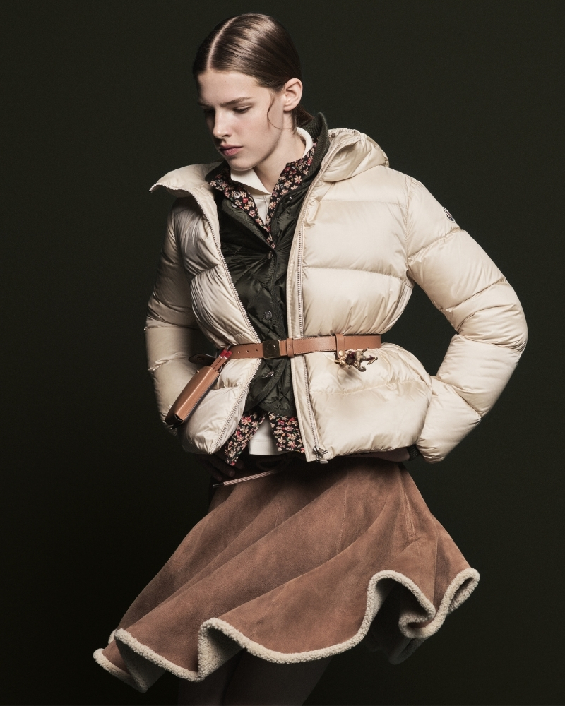 Cream puffer jacket cinched with a brown leather belt%2C layered over a floral top and shearling-trimmed skirt against a dark backdrop%0A