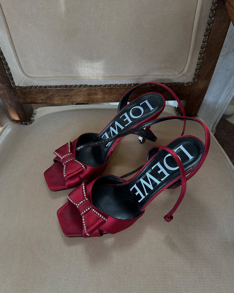 Loewe red satin slingback heels with crystal-embellished bow detail and kitten heel%2C displayed on an upholstered wooden chair indoors