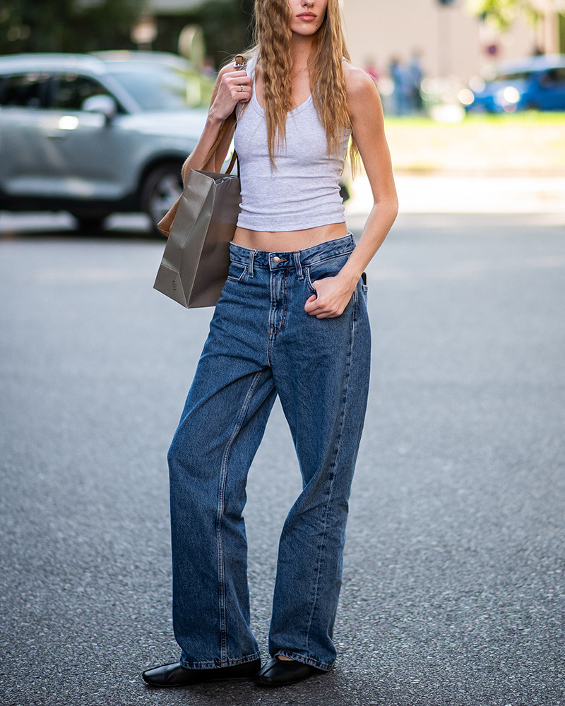 Wide-leg blue jeans styled with a fitted gray tank%2C black ballet flats and tote bag on a city street