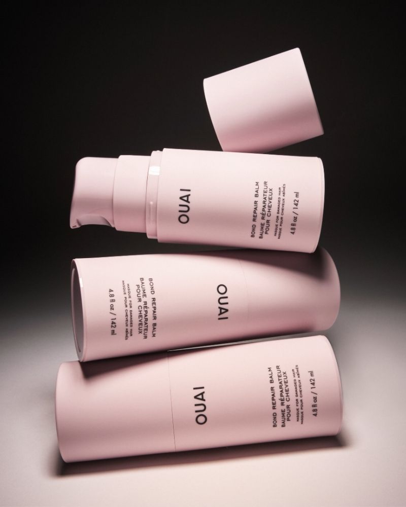 OUAI bond repair hair balm in soft pink bottles%2C stacked in minimalist studio setting with soft gradient lighting