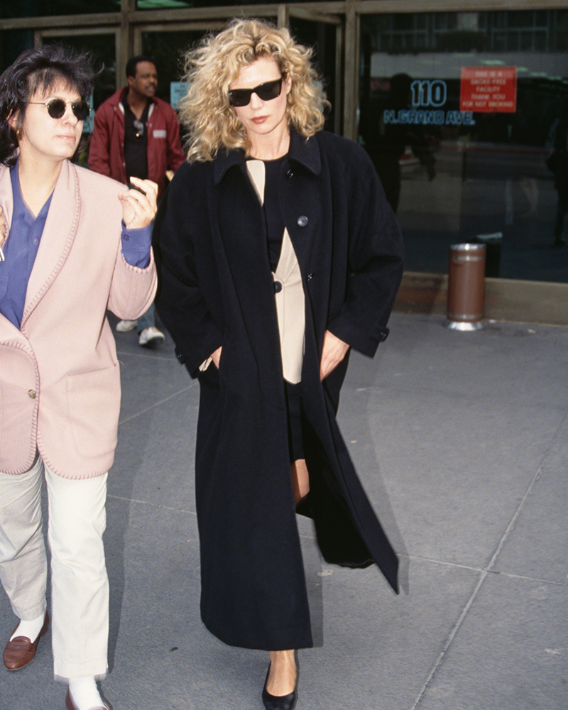 Blonde woman in oversized black wool coat%2C beige blazer and sunglasses with black pumps%2C walking on a New York city sidewalk