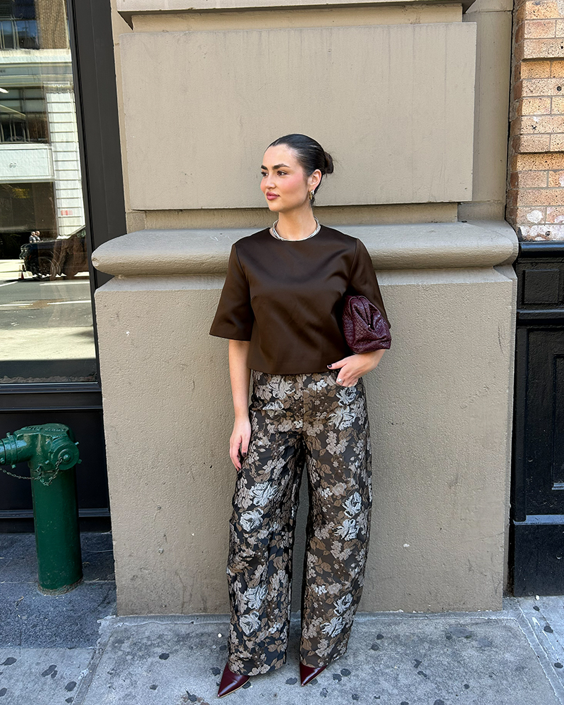 Brown cropped top with floral wide-leg trousers%2C burgundy clutch and pointed pumps styled on a city sidewalk