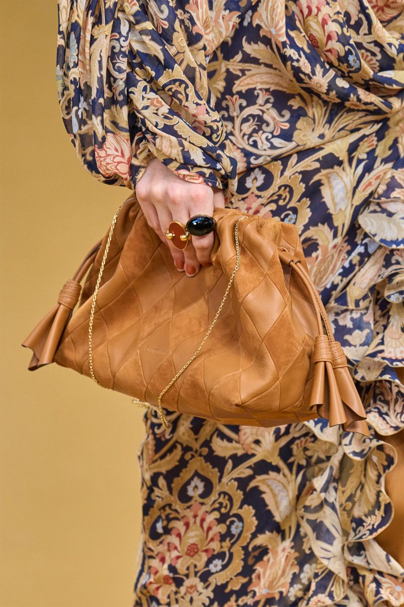 Tan leather quilted drawstring handbag with gold chain and tassel details, styled with a vintage floral print dress on runway backdrop