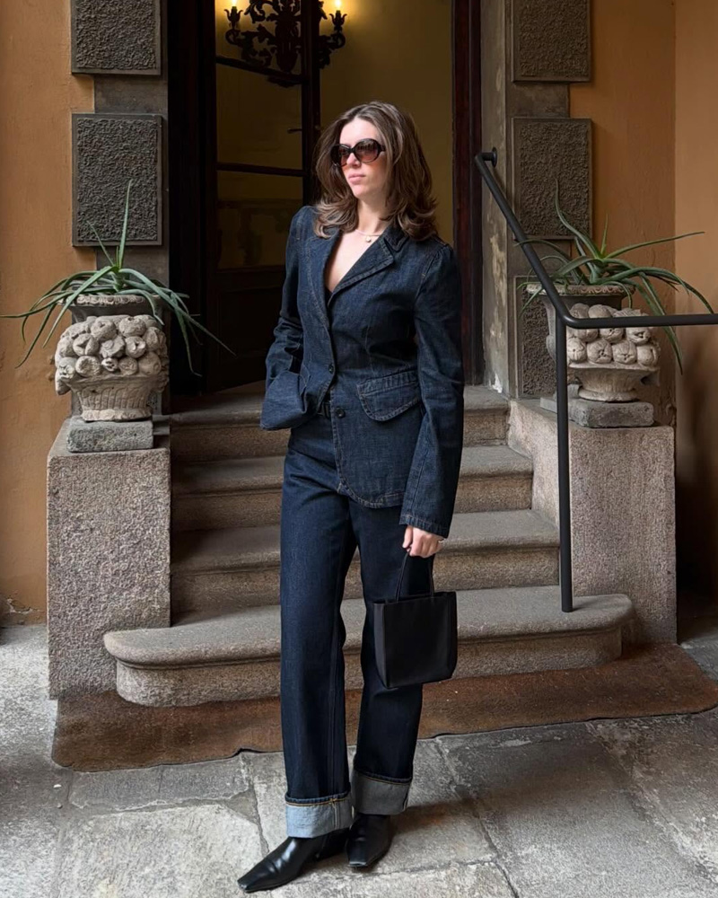 Dark wash denim suit outfit with tailored blazer and wide-leg jeans%2C styled with sunglasses and black leather bag on stone steps outside a townhouse