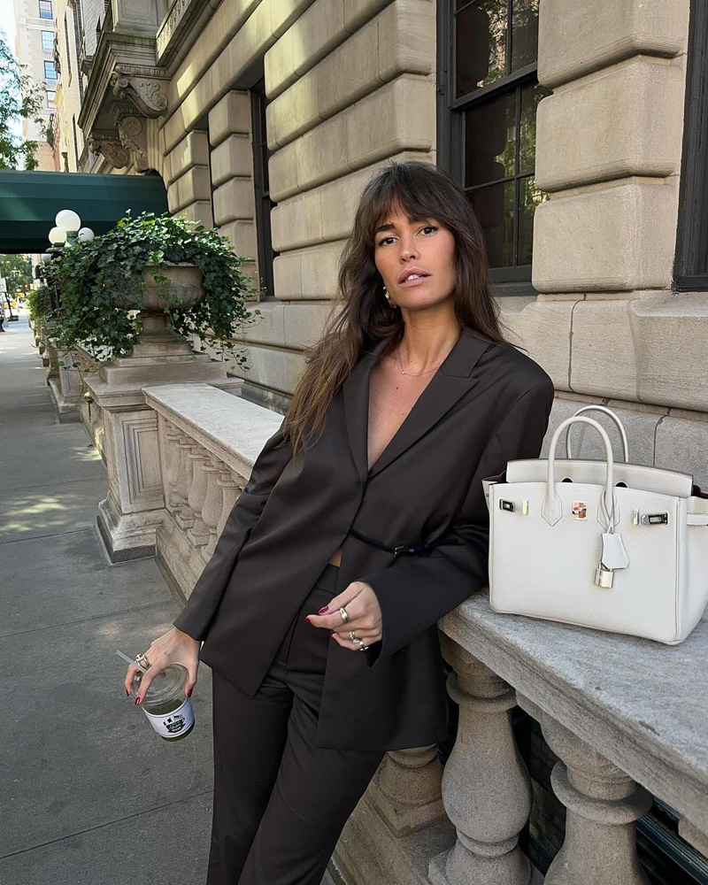 Brown satin blazer and tailored trousers styled with a white Herm%C3%A8s Birkin bag%2C posed against a classic stone building on a city street
