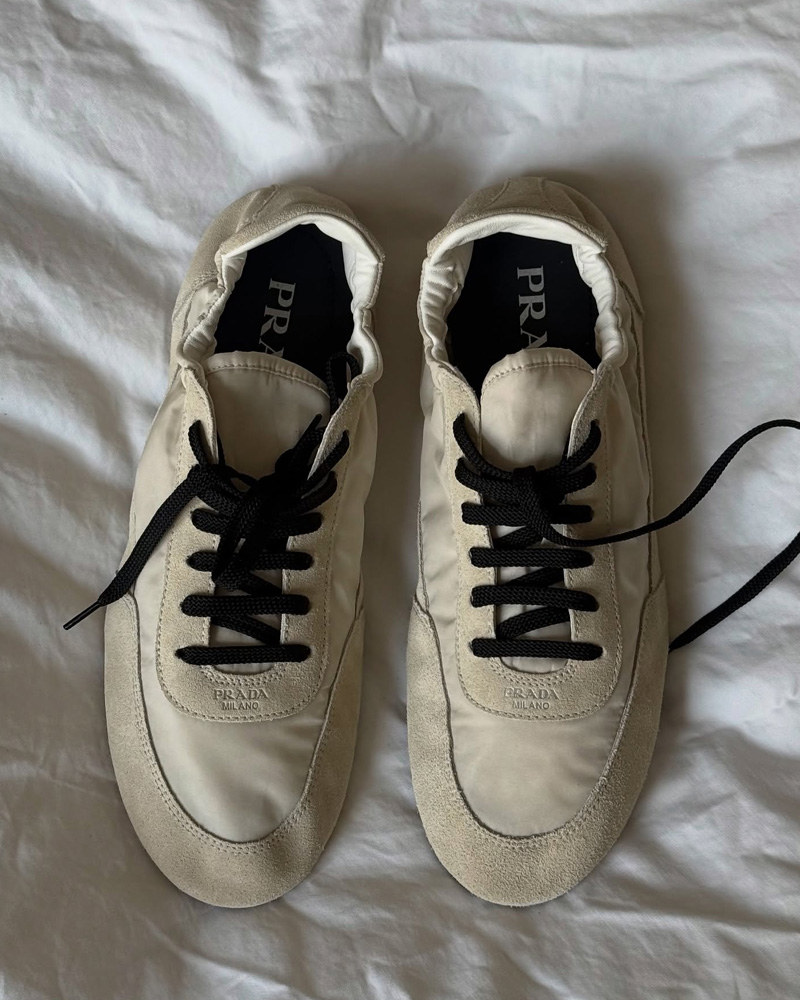 Prada Milano beige nylon and suede sneakers with black laces%2C styled on soft white bedding for a minimal off-duty look